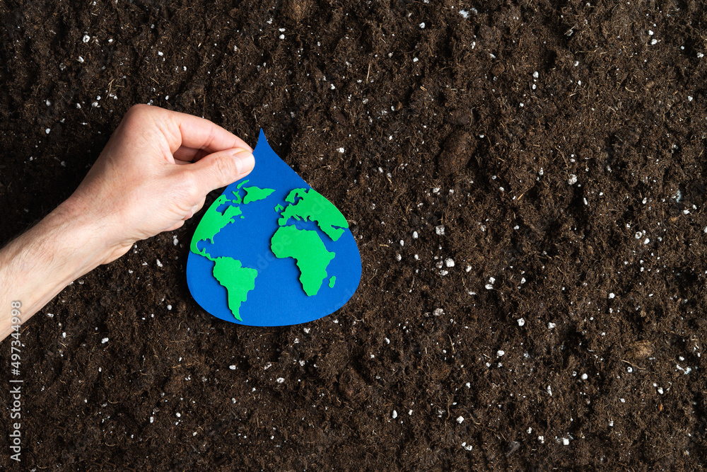 Water drop with world map inside held by a hand on natural earth ...