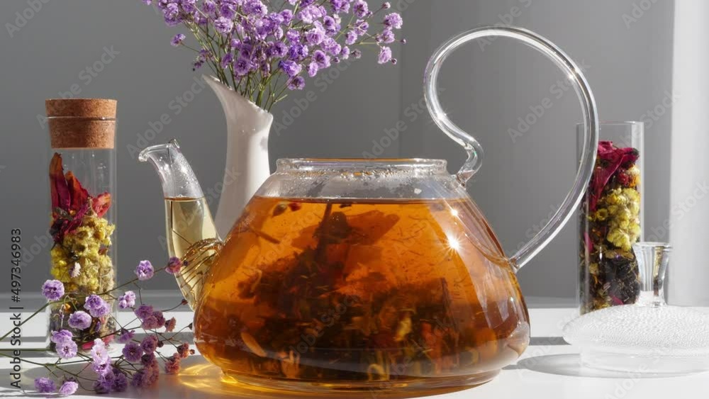 tea with flowers in a transparent glass teapot is brewed in hot water ...