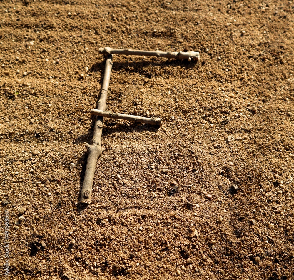 Letter F from small wooden sticks. Capital letter on sandy background ...
