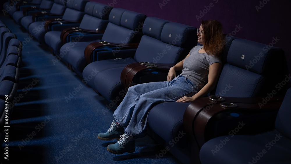 Caucasian red-haired woman sits on the last row in a cinema in an empty ...