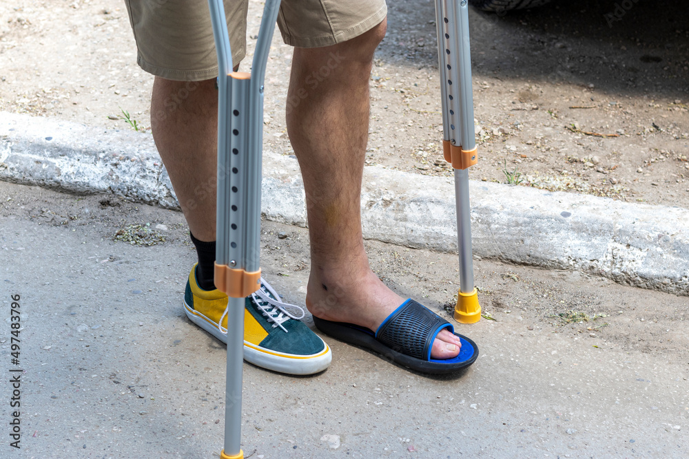 Foto de Legs of young man walking on crutches on sidewalk. Side view ...