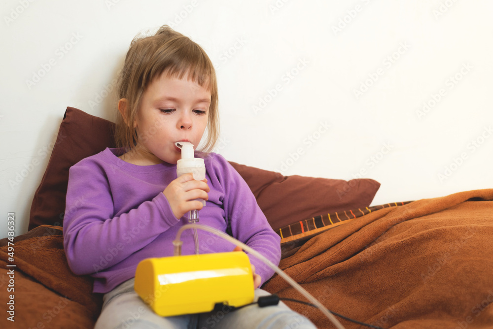 Sick child lies in bed and makes inhalation using a nebulizer ...