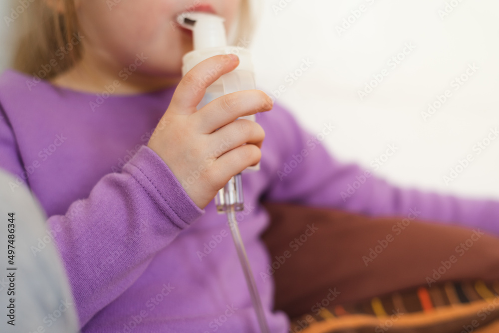 Sick child lies in bed and makes inhalation using a nebulizer. Close-up ...