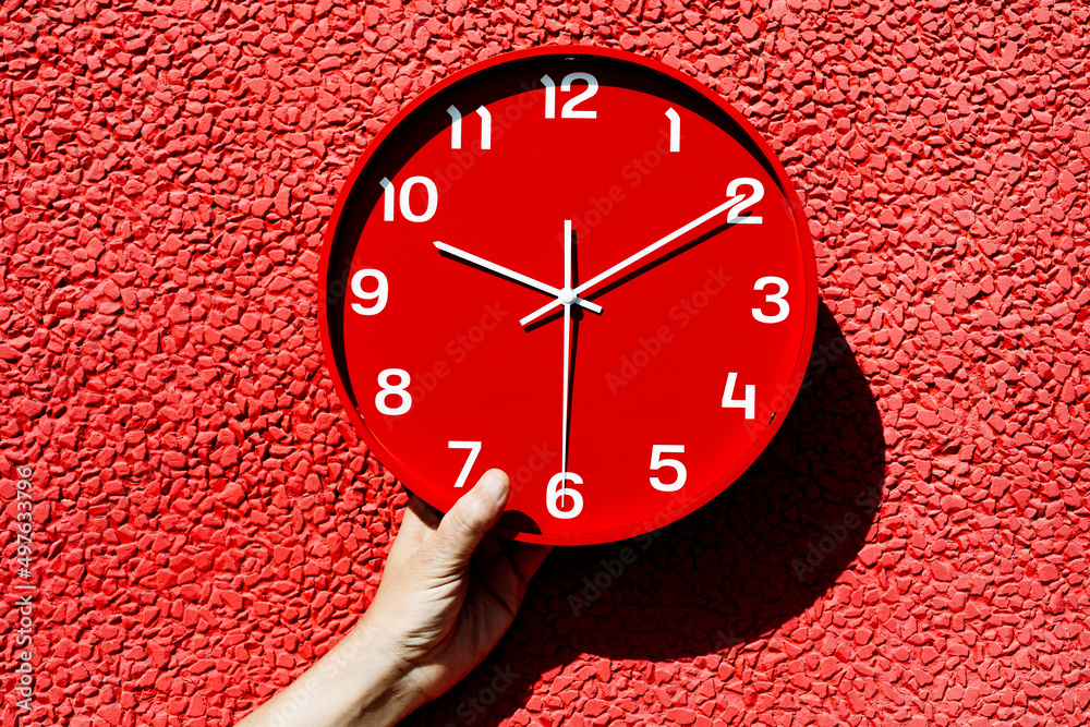 man holding a red clock in front of a red wall Stock Photo | Adobe Stock
