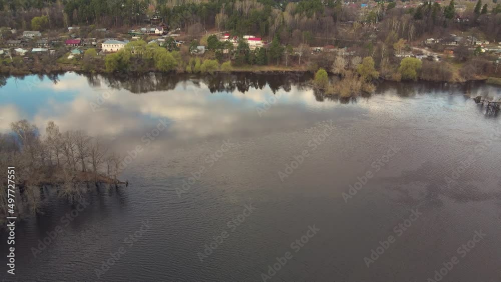 Bright blue sky with clouds reflected in the river, spring flood. Snow ...