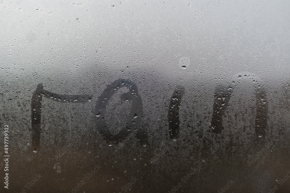 A word Rainy is written on the sweaty foggy window. Water droplets ...