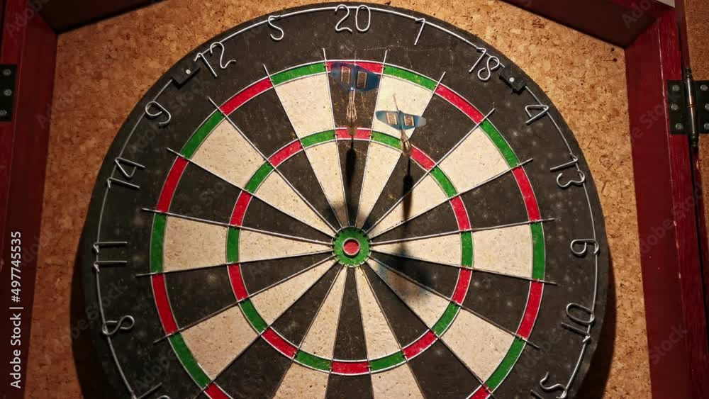 Darts hitting the 20 on a cork dart board twice. Frontal view with a ...