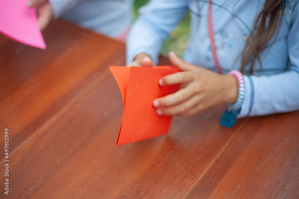 Children make origami out of paper. Child bends colored paper on table ...