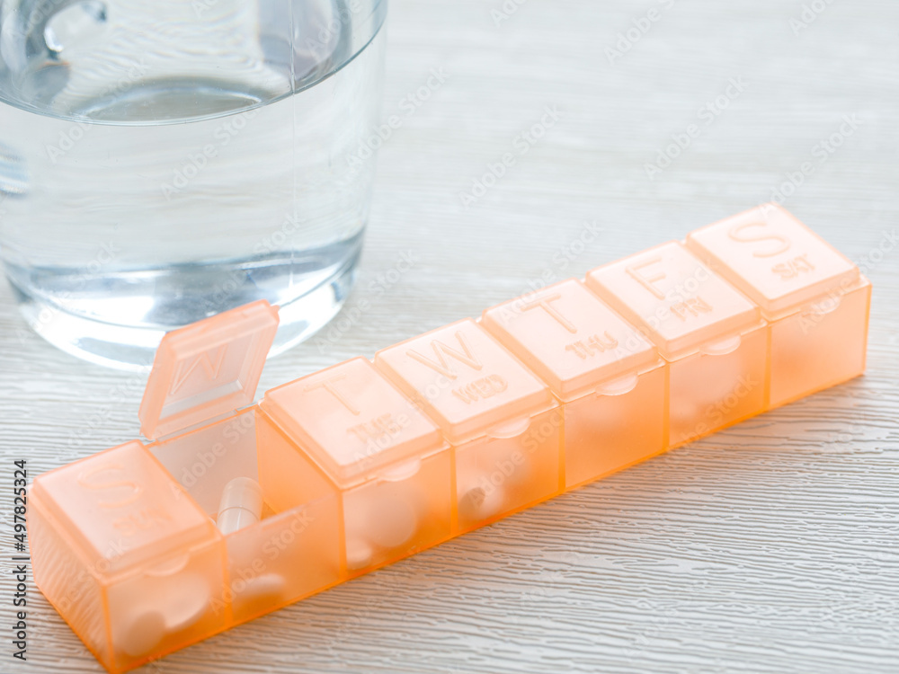 Orange pill box and a glass of water. Prescription drugs in seven day ...