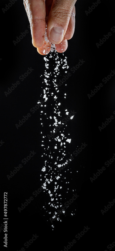 Male hand sprinkling edible salt at black background. Stock Photo ...