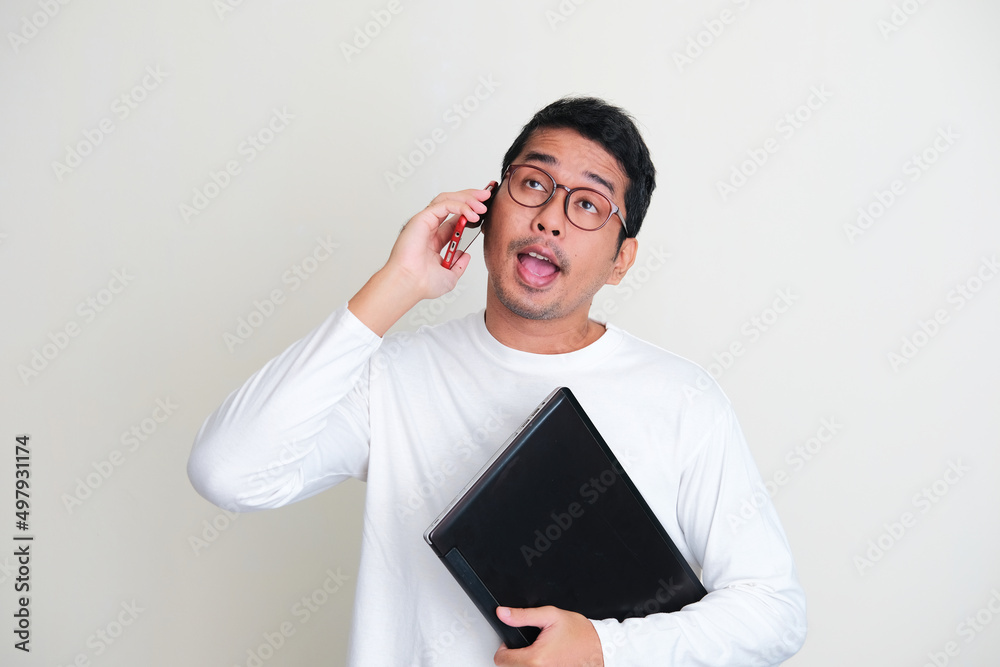 Adult Asian man showing funny ugly face while holding laptop and ...