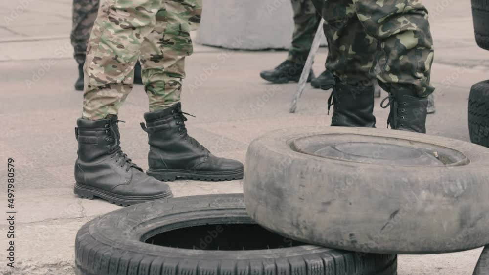 close-up. military feet shod in heavy army boots. old car tires ...