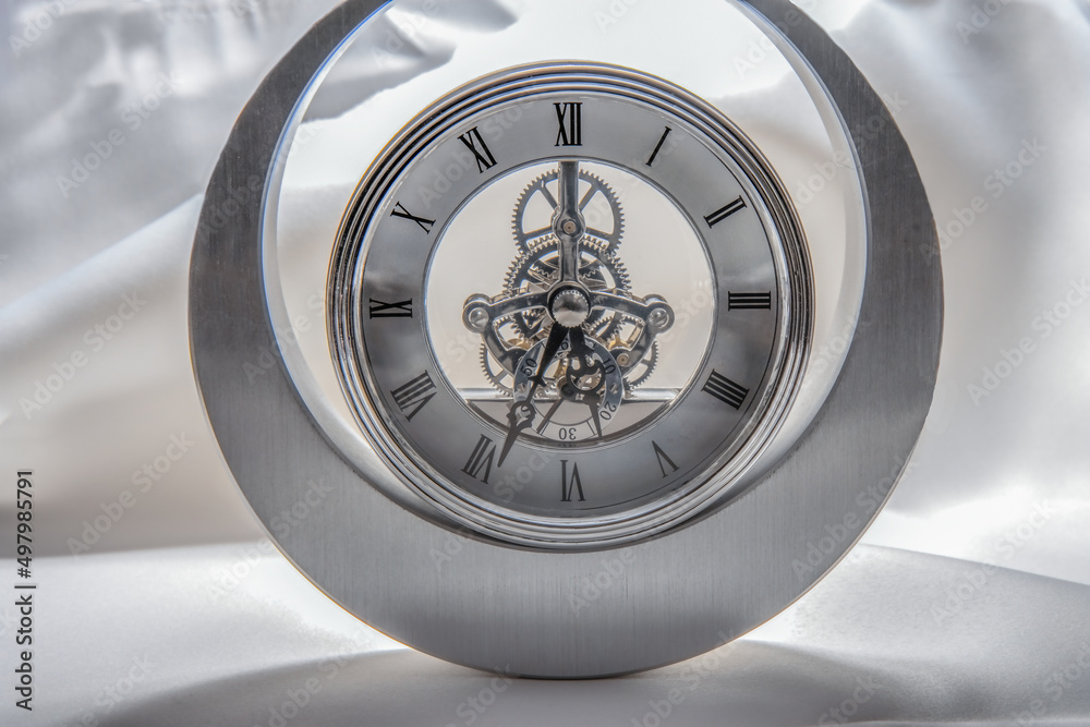 A modern analog clock with a sculpted silver body and see through face ...