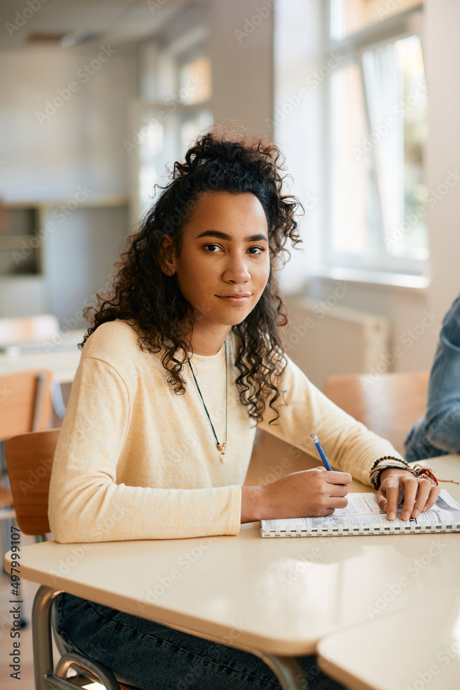 Smiling black high school student writing an exam in the classroom and ...