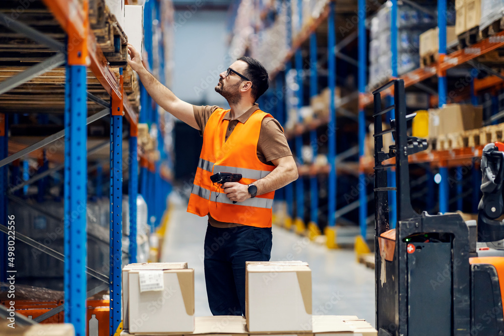 A dispatcher with scanner in hands looking at boxes on shelves in ...