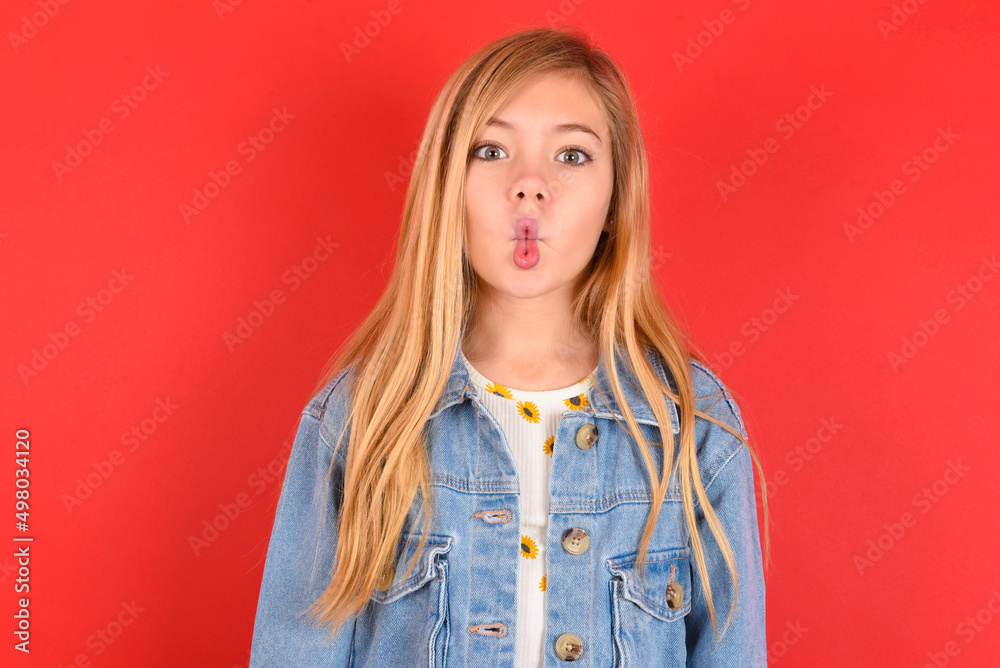 blonde little kid girl wearing denim jacket over red background making ...