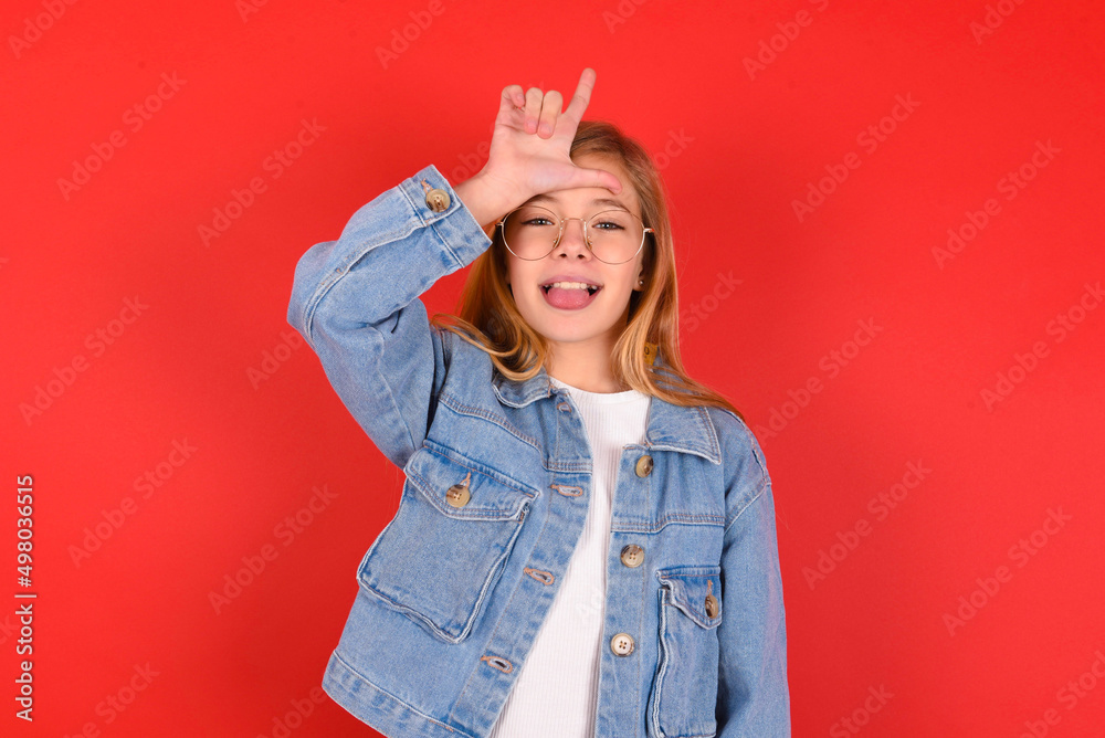 Funny blonde little kid girl wearing denim jacket over red background ...