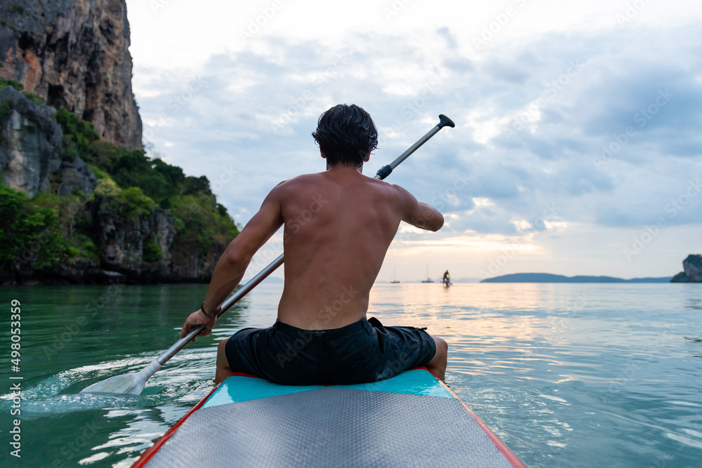 Confidence young Asian man sitting on paddle board and paddleboarding ...