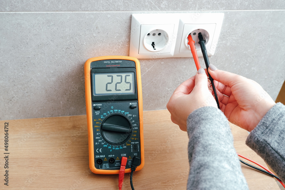 Woman with a multimeter check the voltage of the electrical network ...