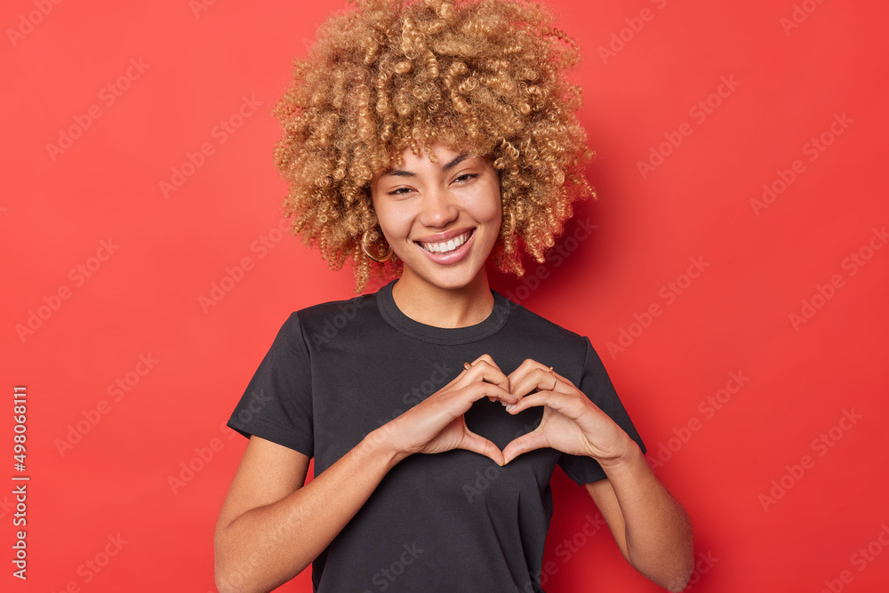 Indoor shot of pretty smiling romantic young woman shapes heart ...