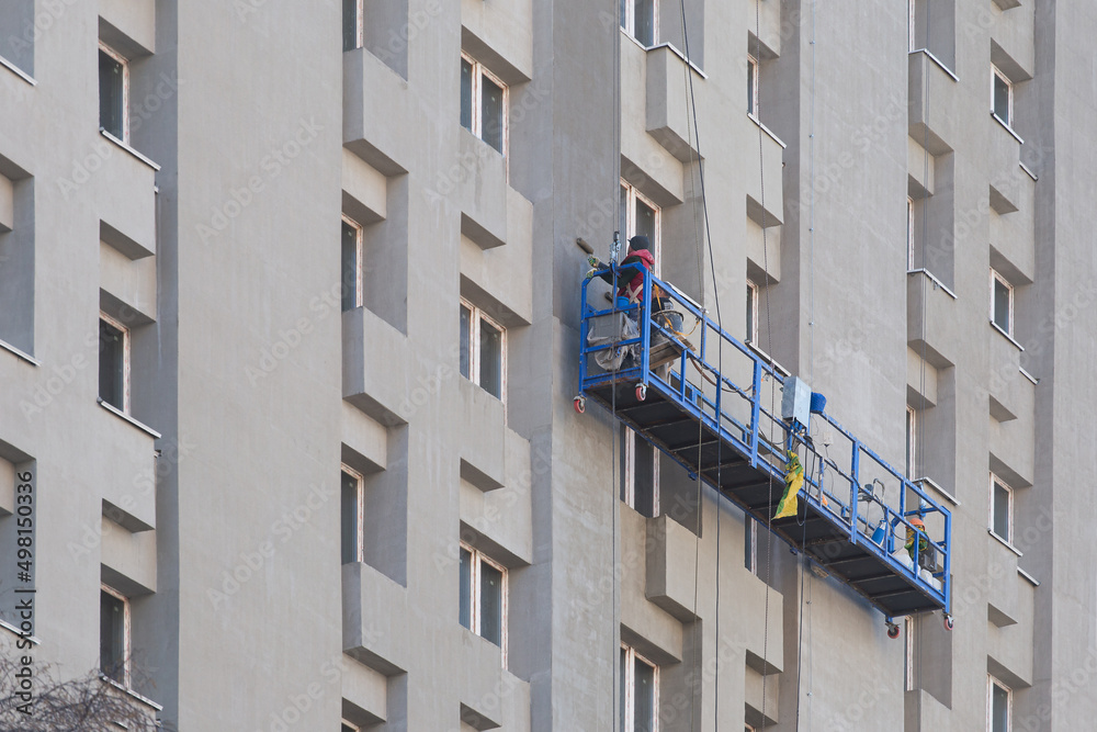 A team of plasterers and painters at a height in a suspended cradle ...
