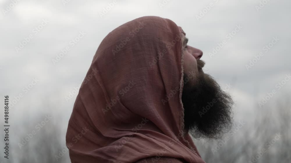 Jesus Christ wearing a brown hood looks down with a serious and sombre ...