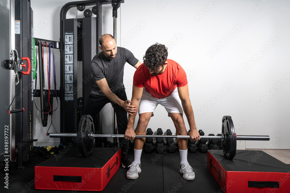 Coach giving support to young man lifting barbell at health club Stock ...