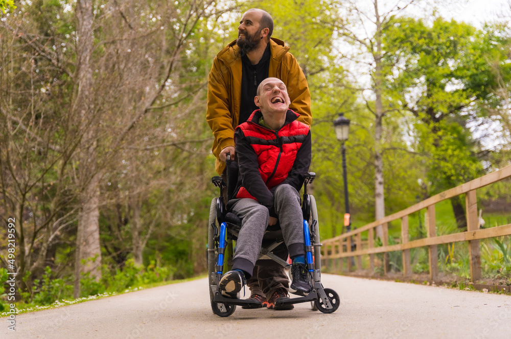 Paralyzed young man in the wheelchair being pushed by a friend in a ...