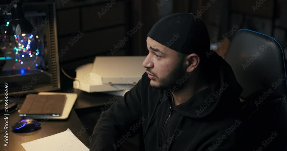 Tired, sleepy, overworked man in cap and sweatshirt works at night in ...
