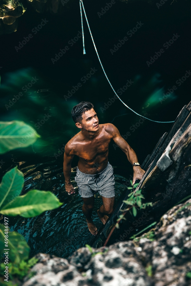 young tan male model climbing from a cenote in Tulum Mexico surrounded ...