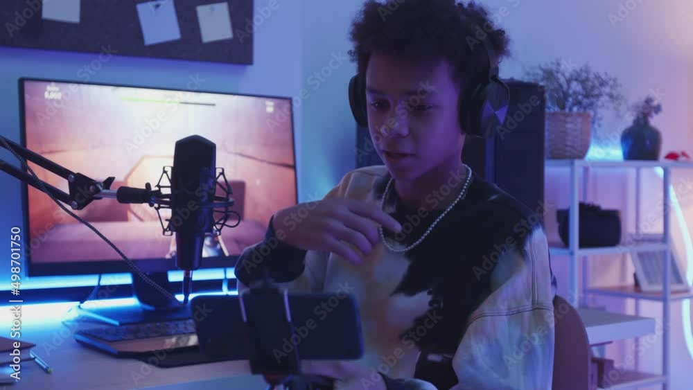 Waist up slowmo of Biracial 14 year old streamer in headphones speaking ...