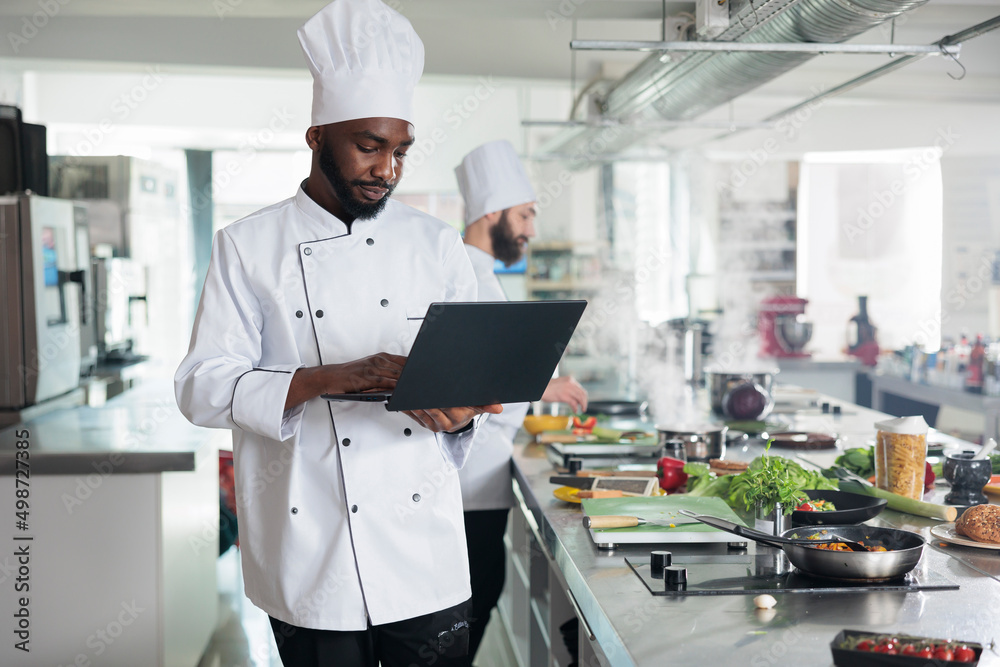 African american head chef with laptop searching for dish recipes on ...