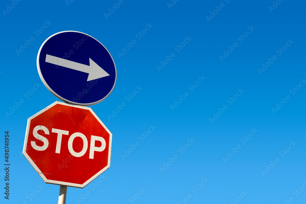 Red stop sign and a blue directional arrow road signs against a blue ...