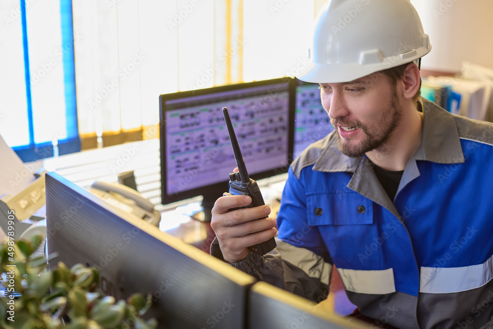 Smiling Caucasian worker in overalls and a helmet uses a walkie-talkie ...