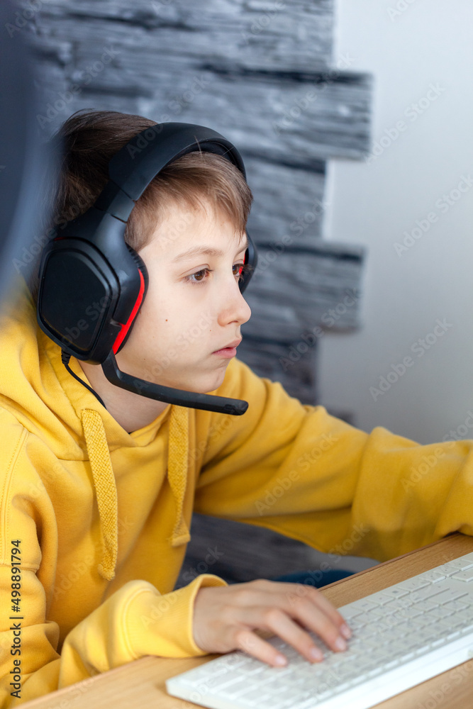Teenage boy in headphones uses computer at home at a distance learning ...