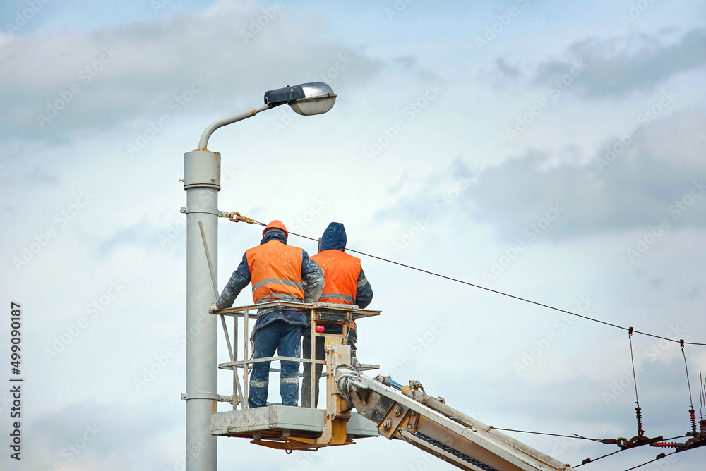 Workers in aerial platform paint street lighting pole. Men in cradle ...