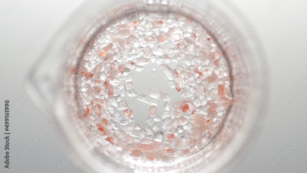 Top view shot of beaker with crystals of brown salt in water on light ...