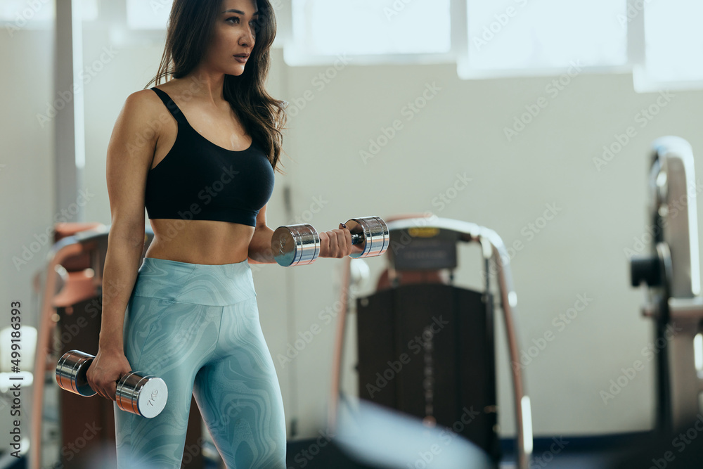 Foto de A fit, strong female bodybuilder is lifting dumbbells and doing ...