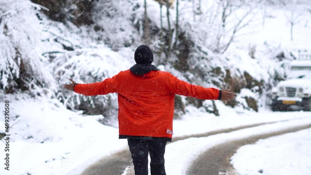 Rear view of an Indian man walking in the snow during snowfall with his ...