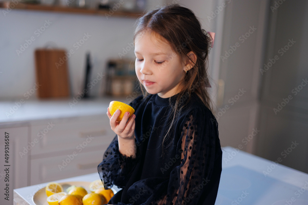 Little baby girl trying and showing lemons in kitchen at home. Child in ...