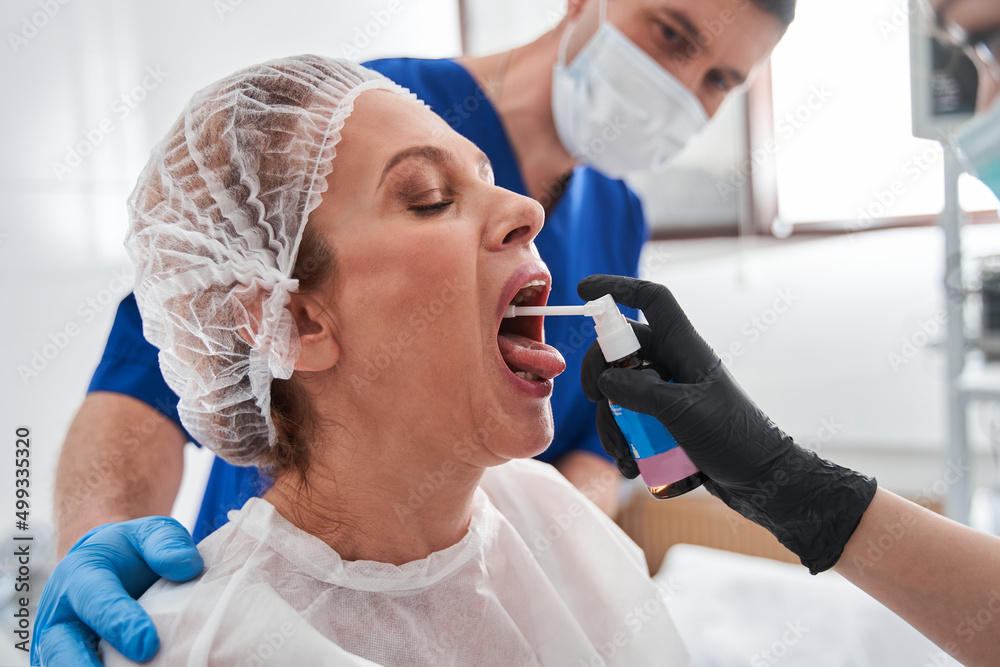 Nurse spraying anaesthesia at the female patient mouth before the ...