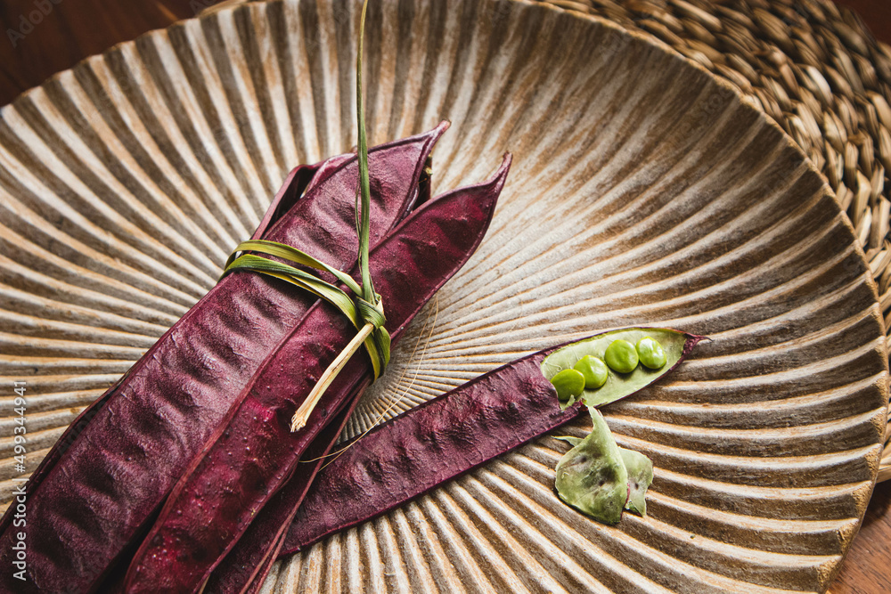 Bundle of purple Guaje bean pods on a plate next to an open bean pod ...