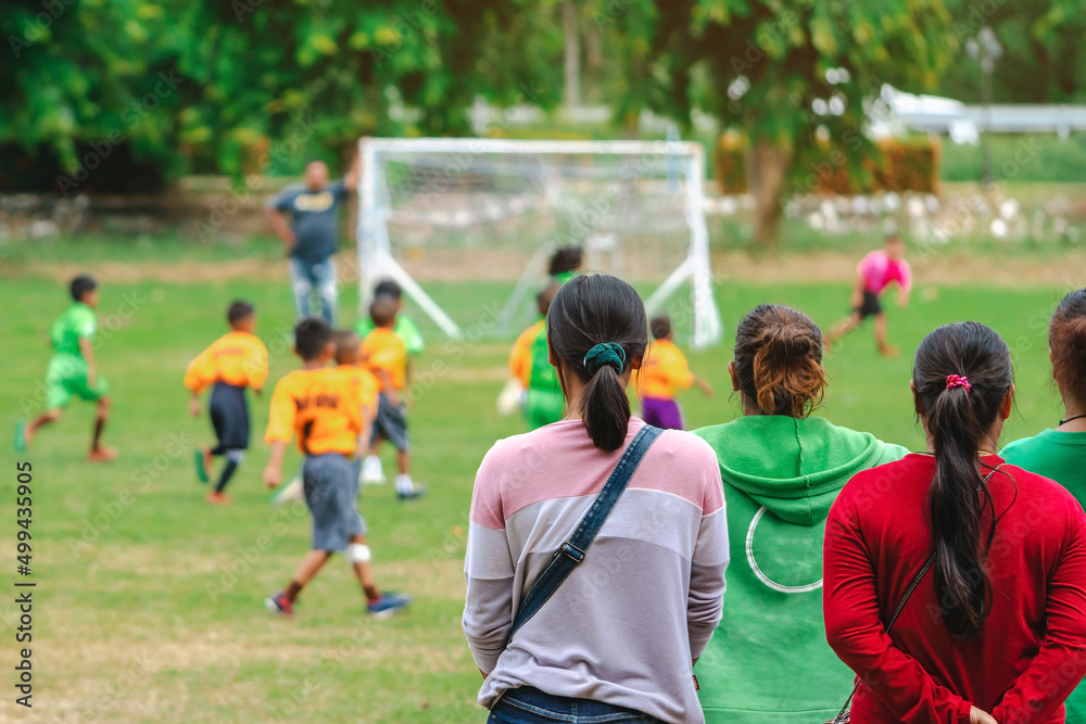 Back view of Moms watch and cheering their sons playing football in ...