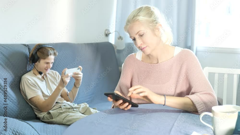 Interested teenage boy and his mother sitting at home table absorbedly ...