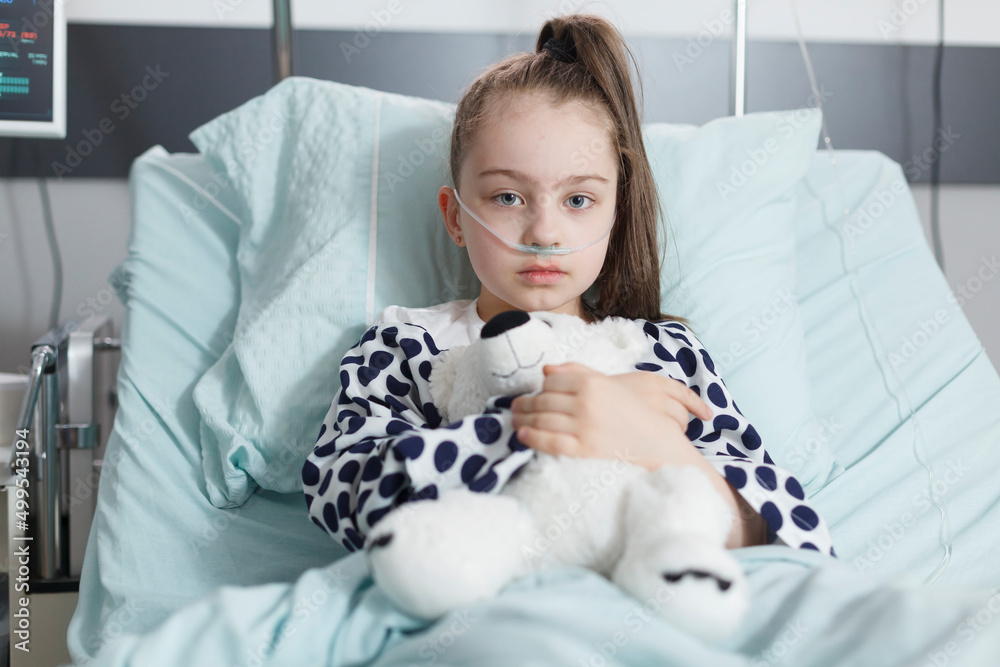 Sick kid holding teddybear and wearing oxygen tube while resting alone ...