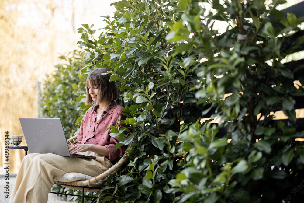 Young woman works on laptop computer while sitting relaxed on chair on ...