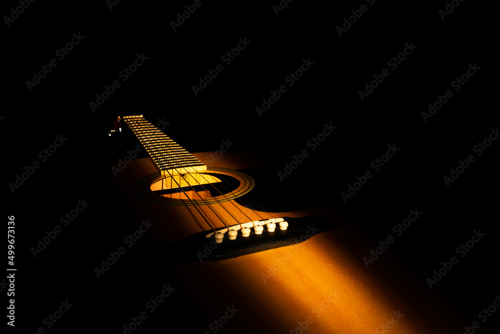 Beam of light illuminates yellow wooden acoustic guitar. Stringed ...