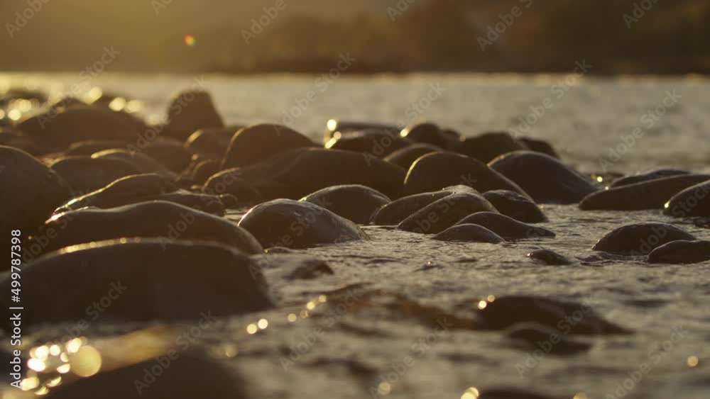 Rocky riverbank washed by waves illuminated by the setting sun. Stones ...