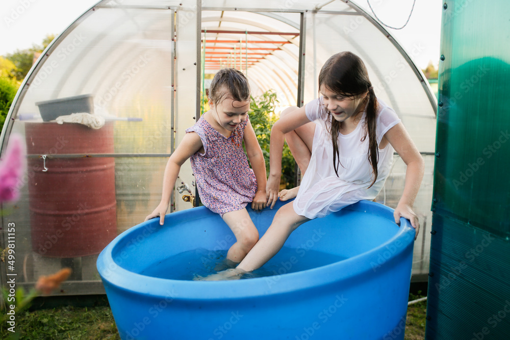 Wet happy children in the garden are bathing in a big blue barrel ...