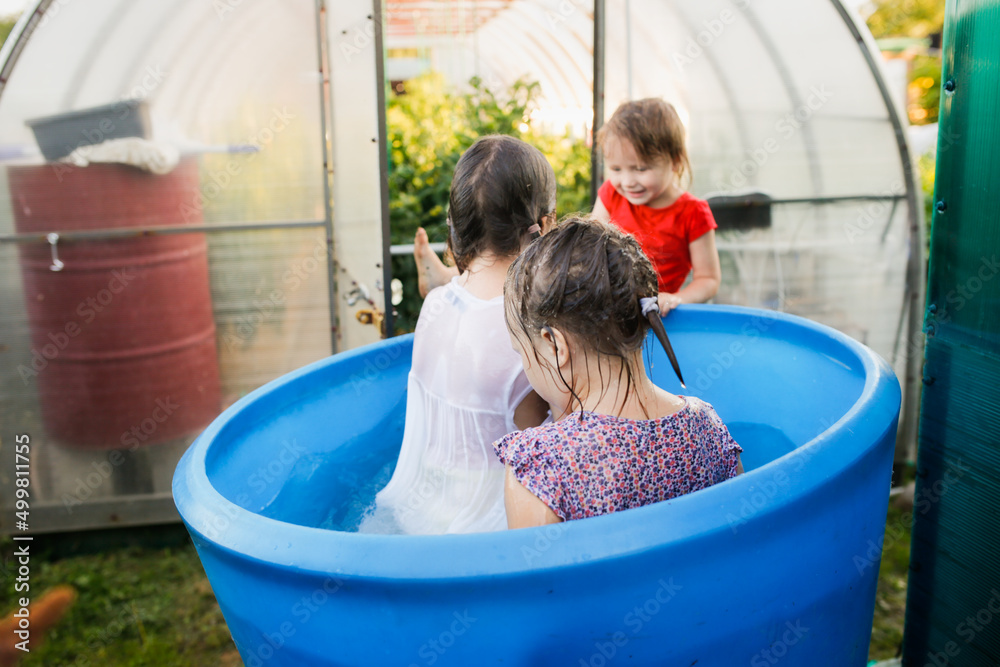 Wet happy children in the garden are bathing in a big blue barrel ...